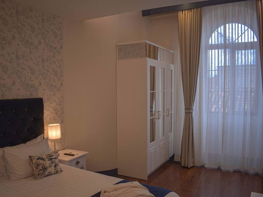 Quarto com cama, mesa de cabeceira, guarda-roupa e janela com cortinas.