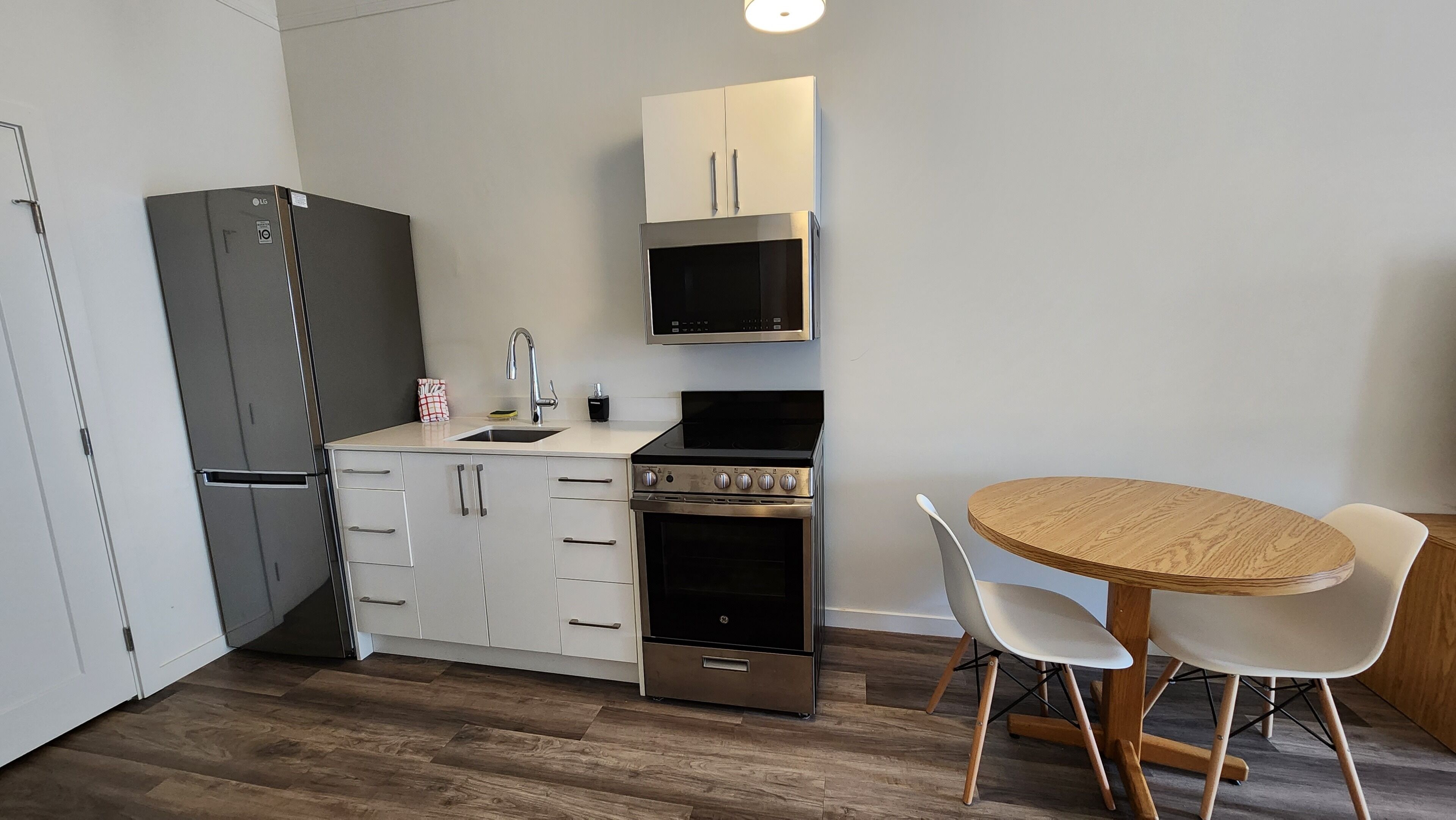 Uma cozinha compacta com geladeira, micro-ondas, fogão e pia. Há uma mesa de jantar com cadeiras.