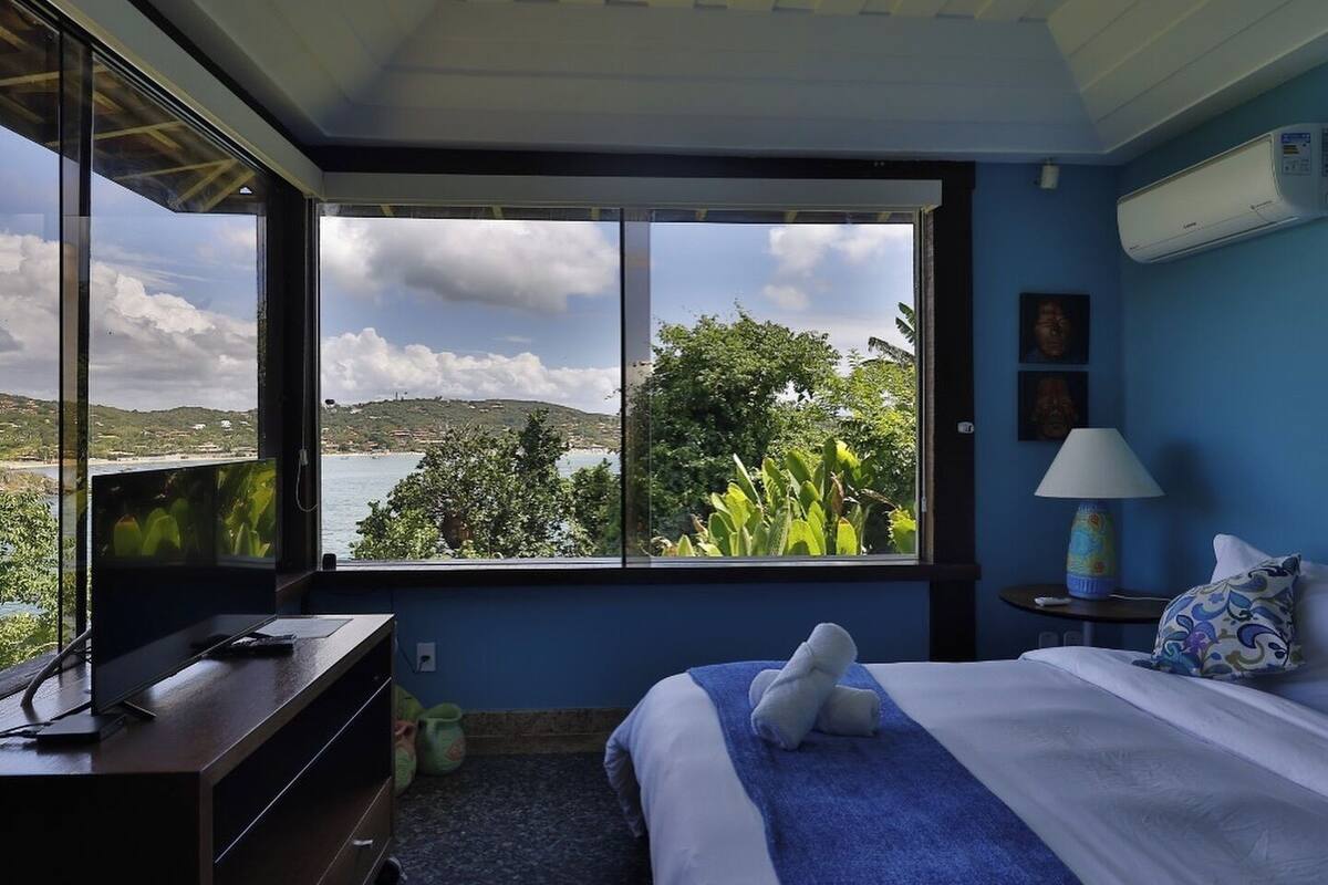 Quarto com uma grande janela, cama, escrivaninha e televisão.