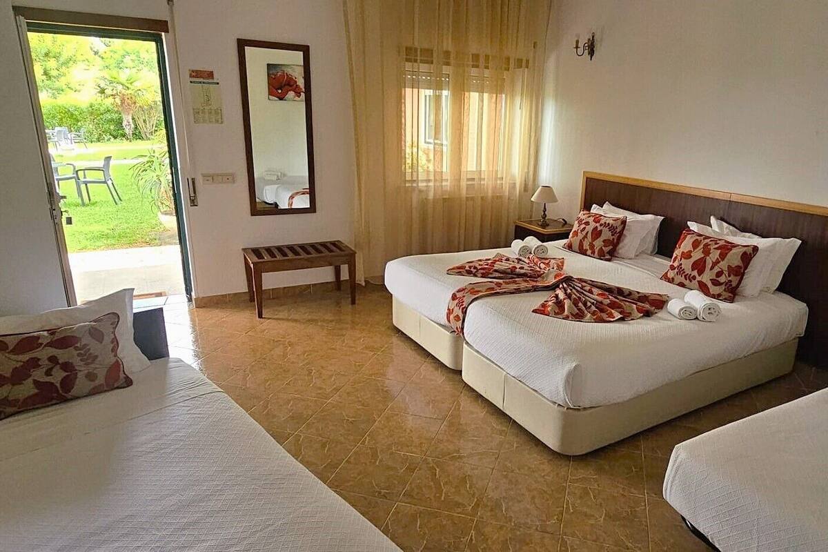 Quarto de hotel com duas camas, um banco e vista para o jardim.