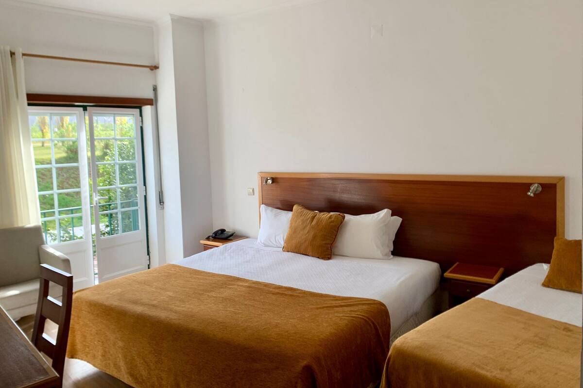 Quarto de hotel com duas camas, uma escrivaninha e uma cadeira.
