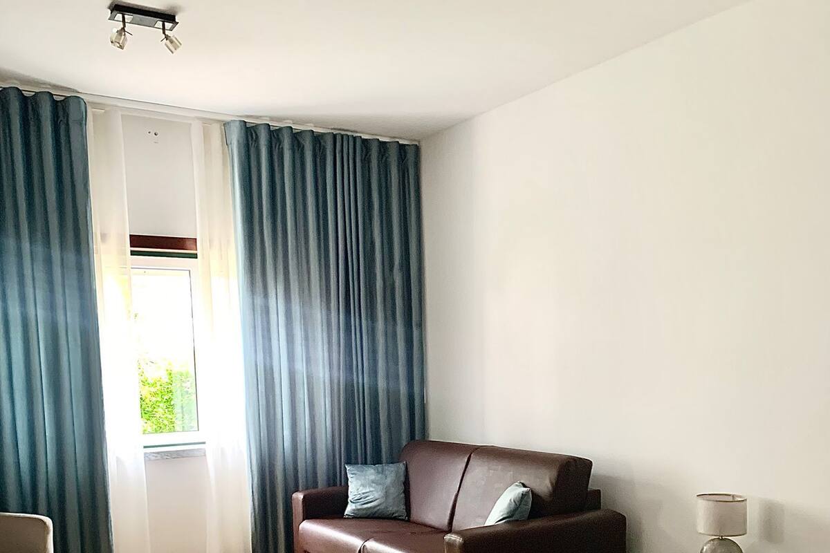 Quarto de hotel com cama, sofá de couro marrom, mesinha de centro com abajur e uma cadeira.