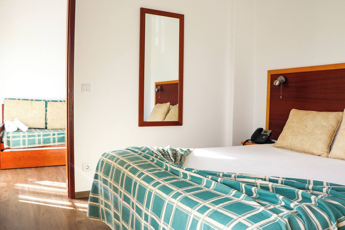 Quarto de hotel com uma cama grande, mesa de cabeceira com telefone e espelho na parede.