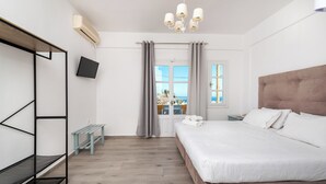 Quarto de hotel com cama, um banco, televisão, janela e vista para o mar.