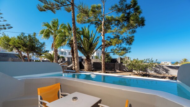 Área na beira da piscina com mesa e cadeiras, cercada por árvores e vista livre para o mar.
