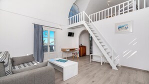 Uma sala de estar ampla com teto alto, uma escada branca, um sofá, uma mesa de centro e vista para o exterior através de uma janela.