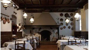 Uma sala de jantar com mesas redondas, luminárias pendentes e uma lareira.