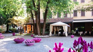 Um pátio com um gazebo, grandes vasos de flores e um edifício com telhado de azulejos.