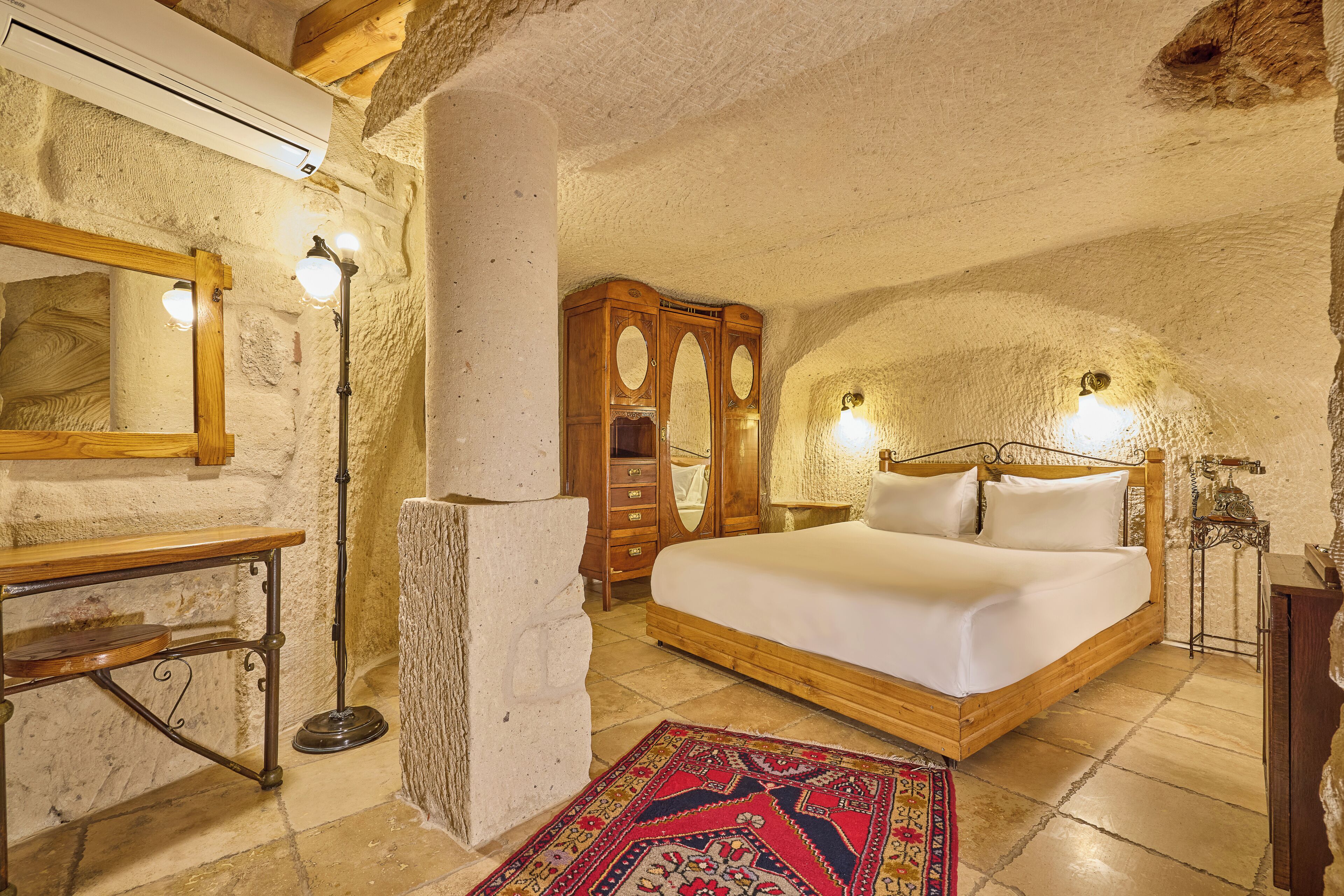 Um quarto rústico com uma cama de madeira, uma mesa de cabeceira, um espelho e uma parede de pedra.