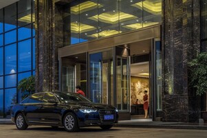 Um edifício moderno com fachada de vidro, um carro estacionado na frente e uma pessoa entrando.