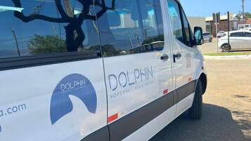 Uma van branca com o logotipo Dolphin e texto indicando sua associação com Noronha - Vila Hotel.