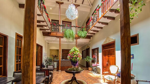 Um lobby amplo com teto alto, uma mesa redonda central decorada com flores e uma escada com guarda-corpo de madeira.