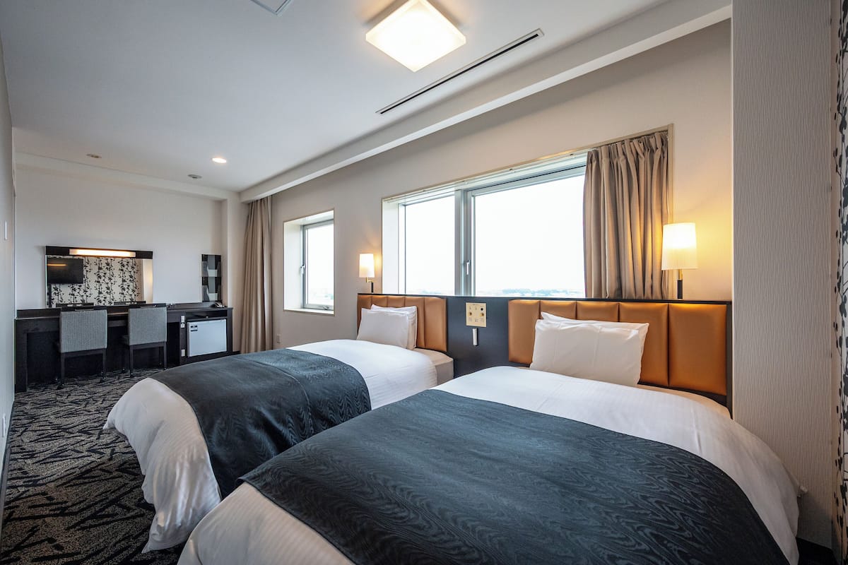Quarto de hotel com duas camas, uma escrivaninha e uma televisão.