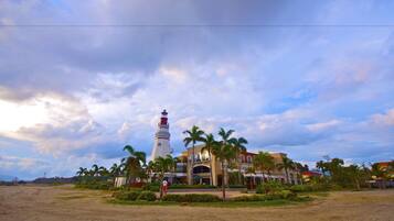 Um hotel à beira-mar com um farol imponente, palmeiras e uma praia arenosa.