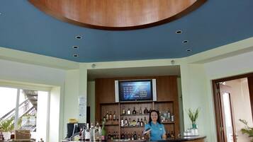 Uma área de bar com design circular em madeira, uma tela de televisão e um bartender.