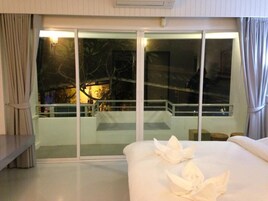 Quarto de hotel com uma cama grande, uma varanda com guarda-corpo e vista para o céu noturno e árvores.
