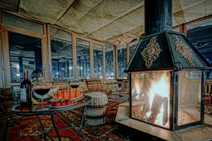 Um quarto aconchegante com uma lareira grande, uma mesa de jantar com comida e bebidas, e janelas amplas que oferecem vista da cidade à noite.