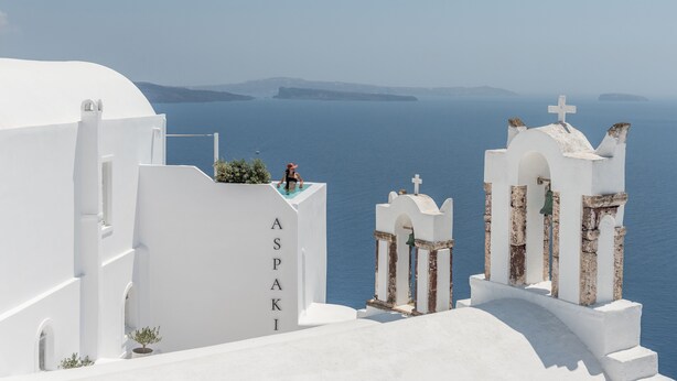 Um edifício branco com a palavra "ASPAKI" na lateral, com vista para um corpo d'água e paisagens distantes.