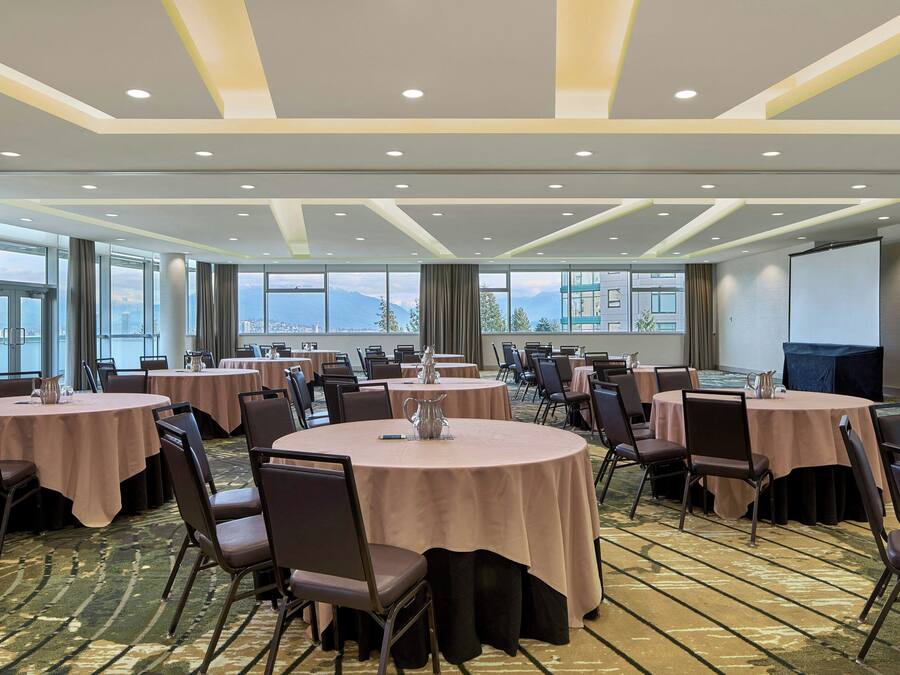 Uma sala de conferências com várias mesas redondas, cadeiras e uma tela de projeção.