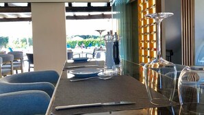 Um restaurante com área de bar, banquetas, uma taça de vinho e saleiro e pimenteiro no balcão.