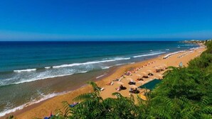 Uma praia com fileiras de espreguiçadeiras e guarda-sóis, céu azul límpido e o oceano.