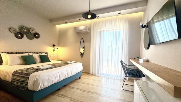 Quarto de hotel moderno com uma cama grande, uma escrivaninha, televisão de tela plana e uma janela ampla com cortinas.