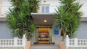 Entrada de hotel com uma placa indicando "H. ANIBAL" e uma placa com "HOSTAL ANIBAL". Há degraus que levam à entrada, e o edifício tem fachada de pedra com azulejos decorativos.