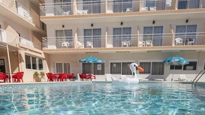 Piscina com decoração de cisne, cadeiras vermelhas e guarda-sóis.