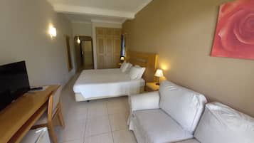 Quarto de hotel com cama, sofá, escrivaninha com televisão e um quadro na parede.