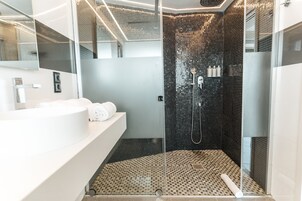 Um banheiro moderno com chuveiro em gabinete de vidro, pia branca e piso ladrilhado.