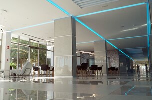 Um lobby moderno com piso refletivo, áreas de estar e iluminação azul de destaque.