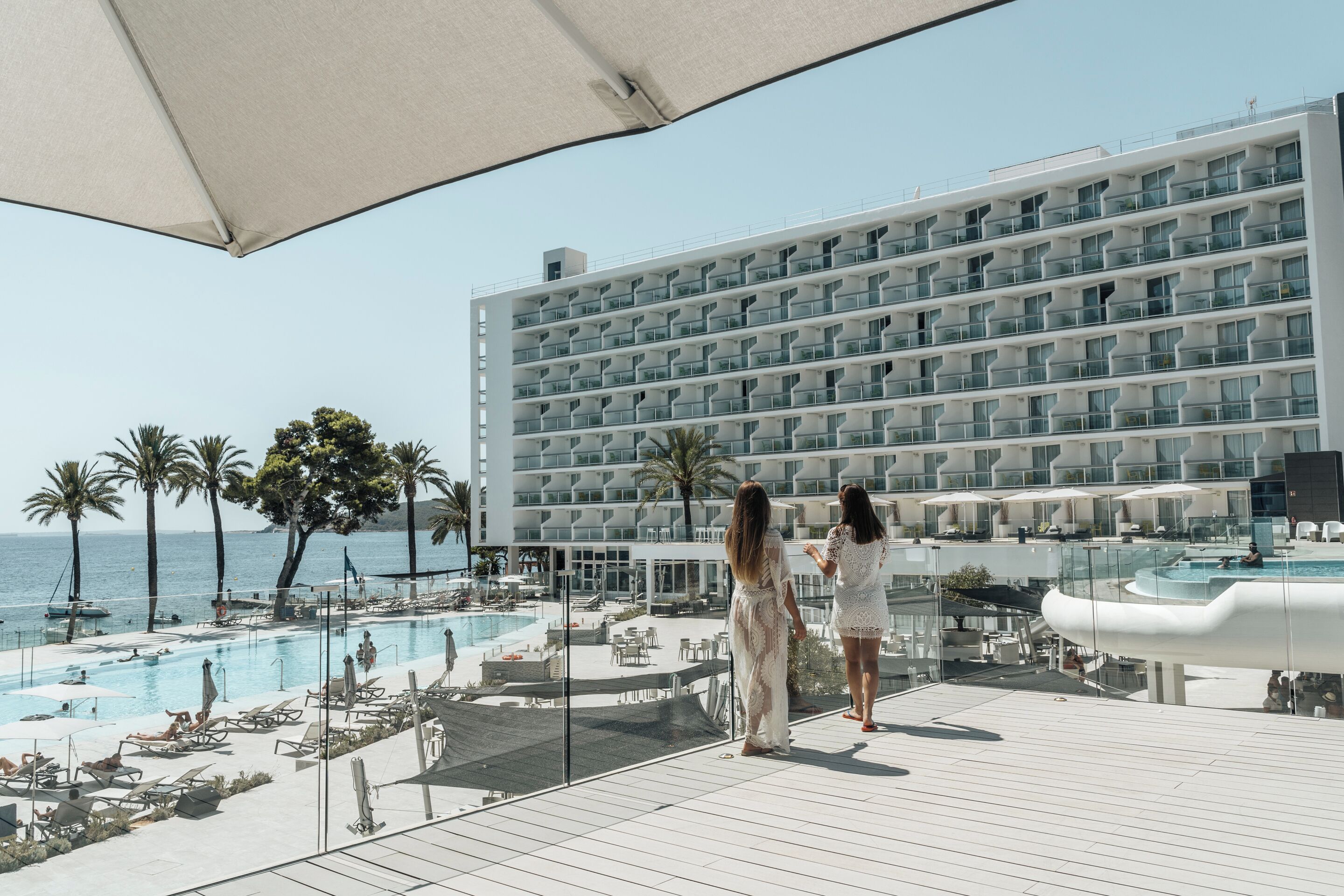 Um hotel com piscina, palmeiras e vista para o mar.