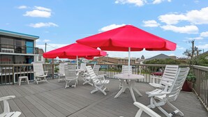 Terraço com cadeiras de lounge brancas e guarda-sóis vermelhos, com vista para um horizonte urbano.