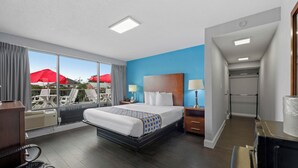 Quarto de hotel com uma cama grande, uma escrivaninha, uma cadeira e vista para área externa com guarda-sóis vermelhos.