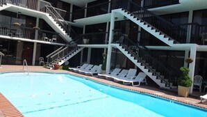 Piscina com cadeiras de descanso brancas e escadaria que leva a um andar superior.