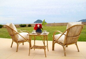 Conjunto de cadeira e mesa de vime em um pátio com vista para o mar.