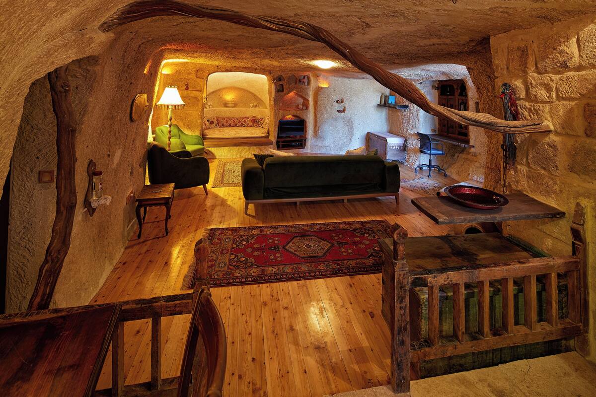 Um interior rústico com soalho de madeira, um sofá verde, uma mesa de madeira e uma parede de pedra.