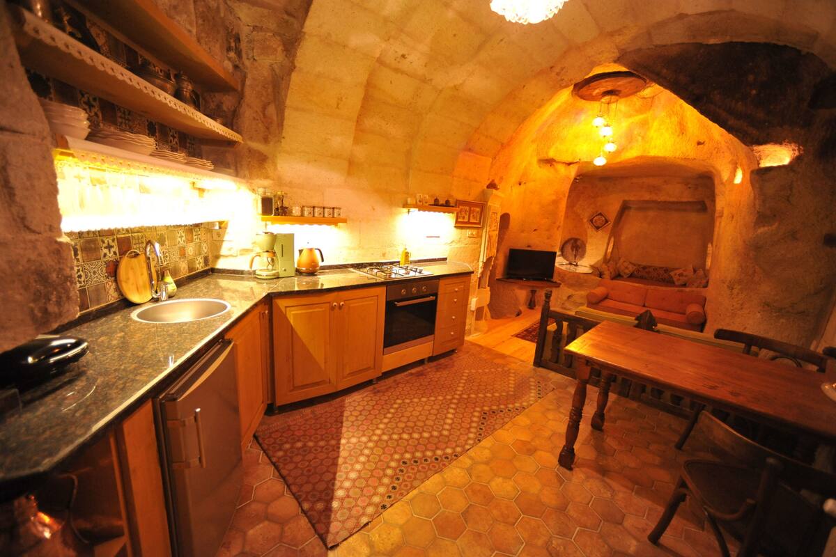 Uma cozinha com parede de pedra, armários de madeira, pia, fogão e área de jantar com mesa e cadeiras.