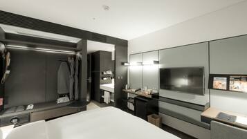 Quarto de hotel moderno com uma cama, toucador com espelho, televisão e secretária com cadeira.