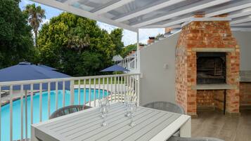 Um pátio externo com piscina, forno de tijolos e área de estar coberta.
