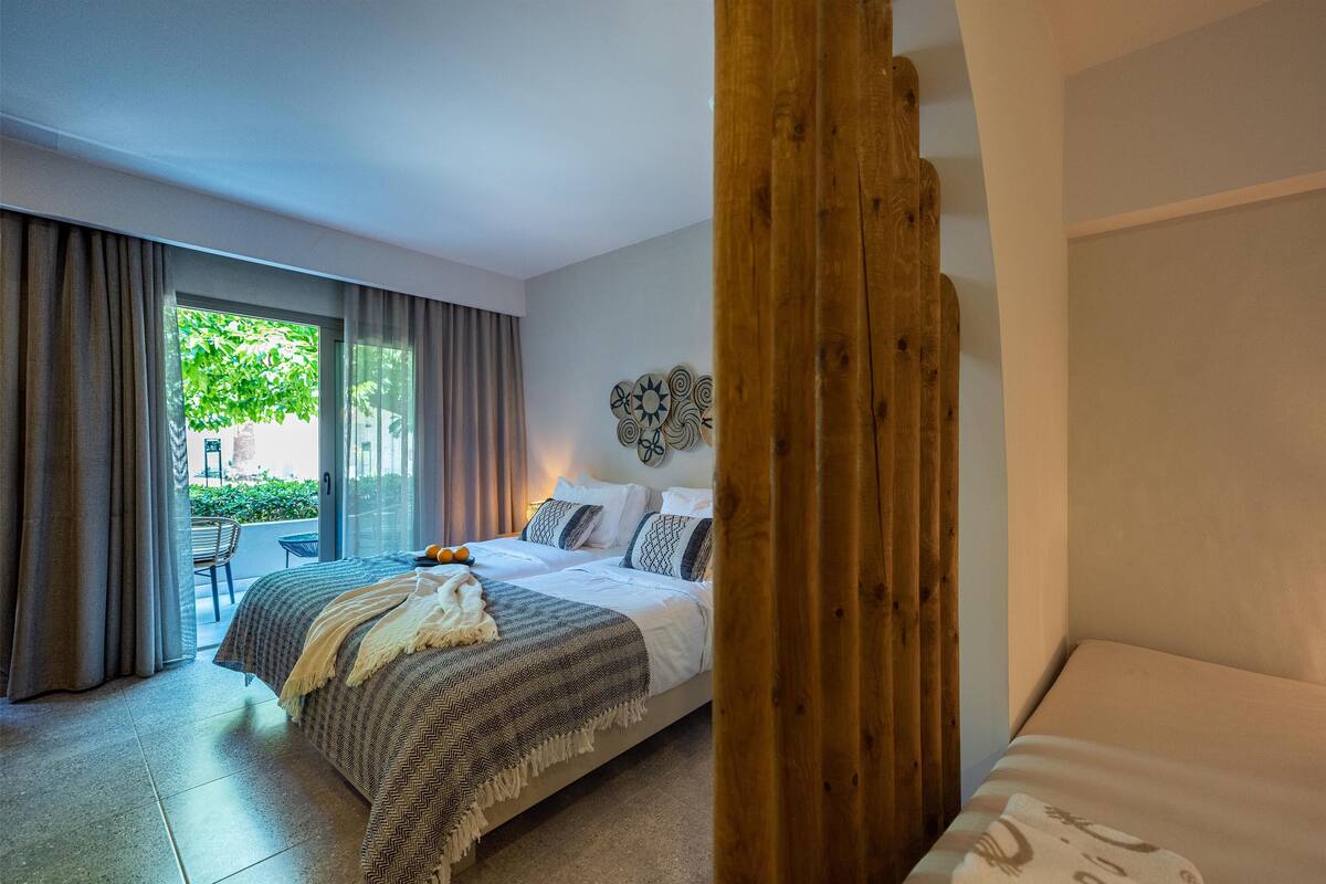 Quarto com cama, porta de madeira e vista para uma varanda com cadeira.