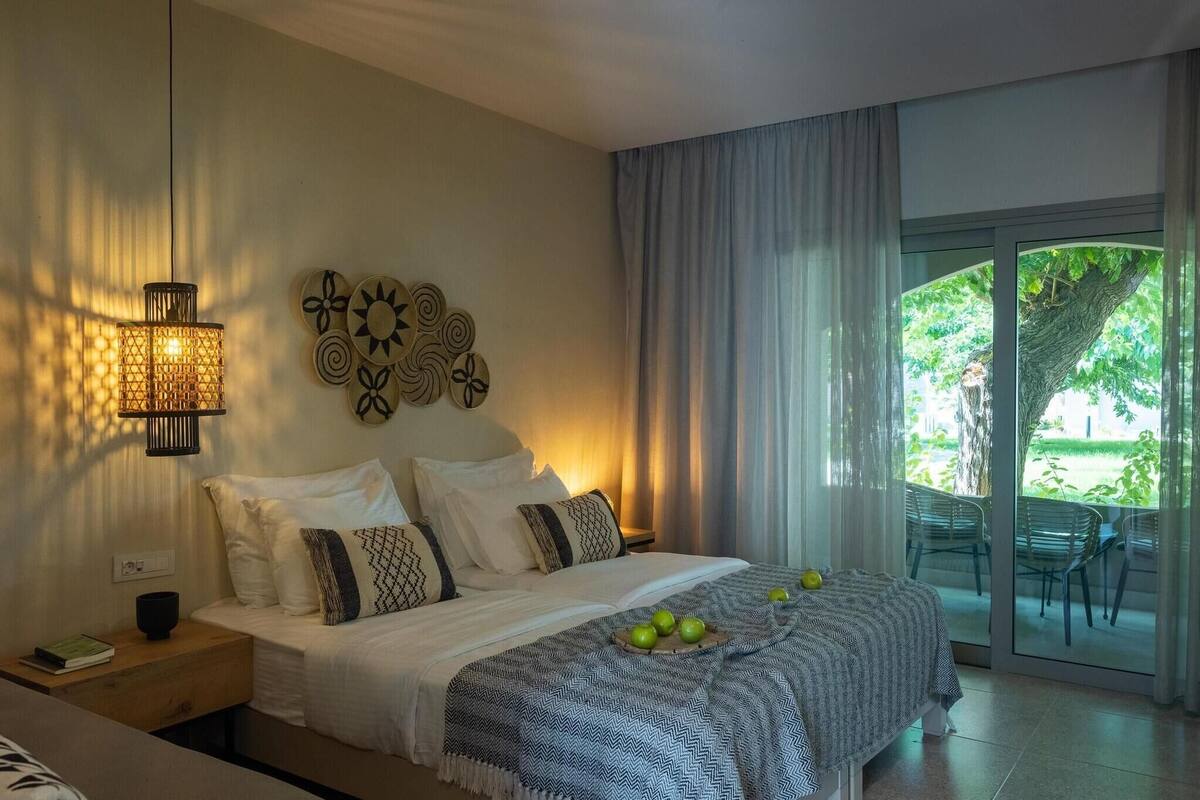 Quarto com cama, mesa de cabeceira, arte decorativa na parede e vista para o exterior.