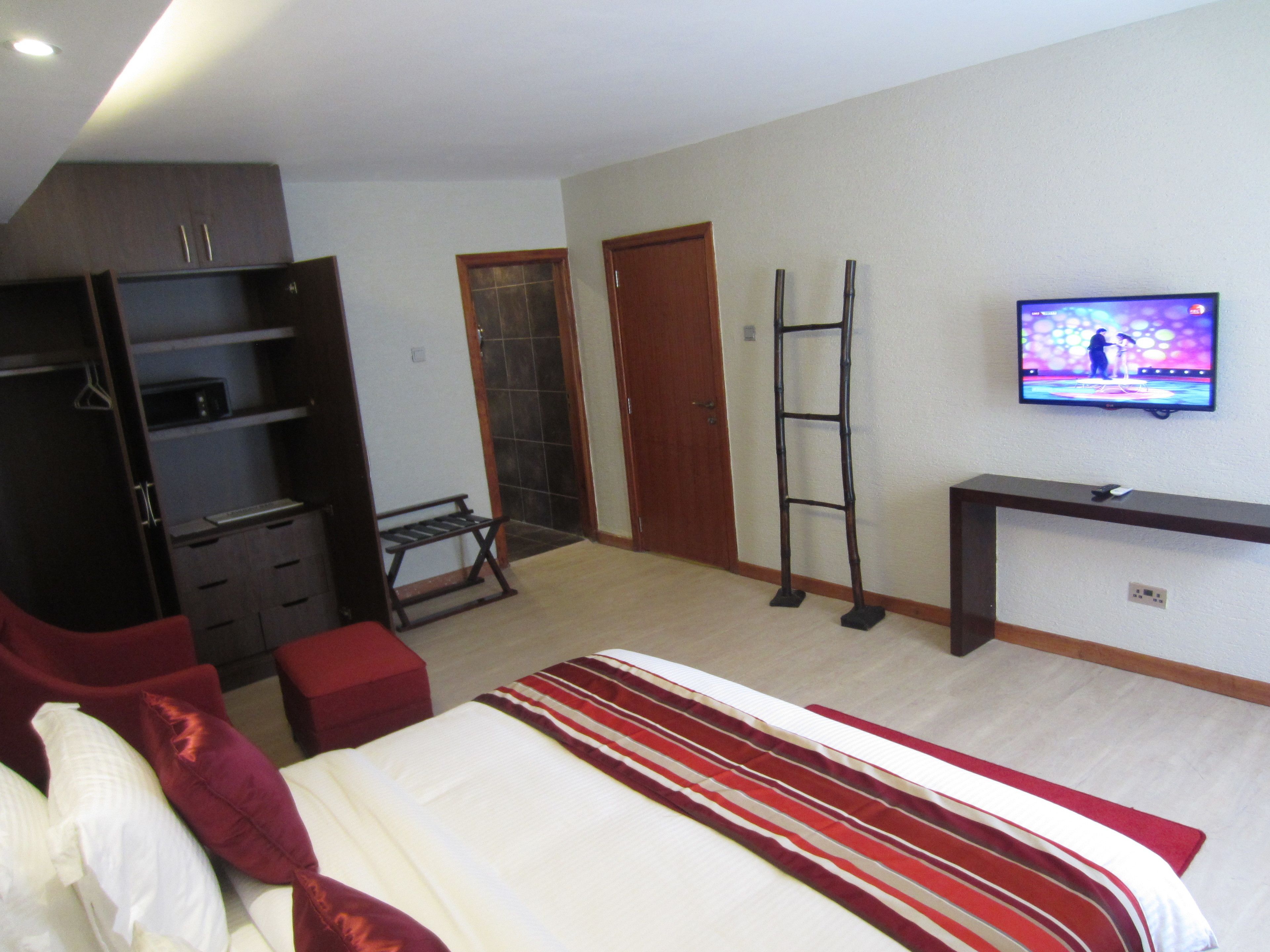 Quarto com cama, escrivaninha, televisão, guarda-roupa e uma cadeira.