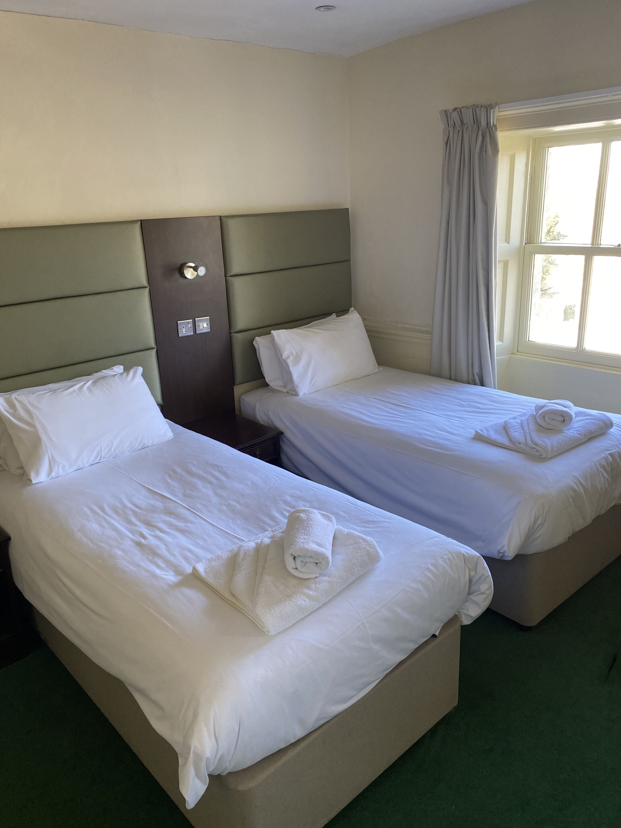 Quarto de hotel com duas camas, cada uma com roupa de cama e toalhas brancas.