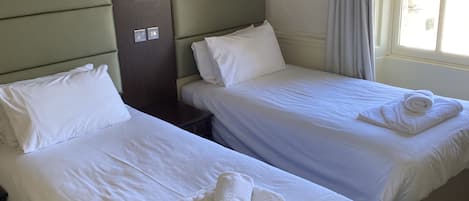 Quarto de hotel com duas camas, cada uma com roupa de cama e toalhas brancas.
