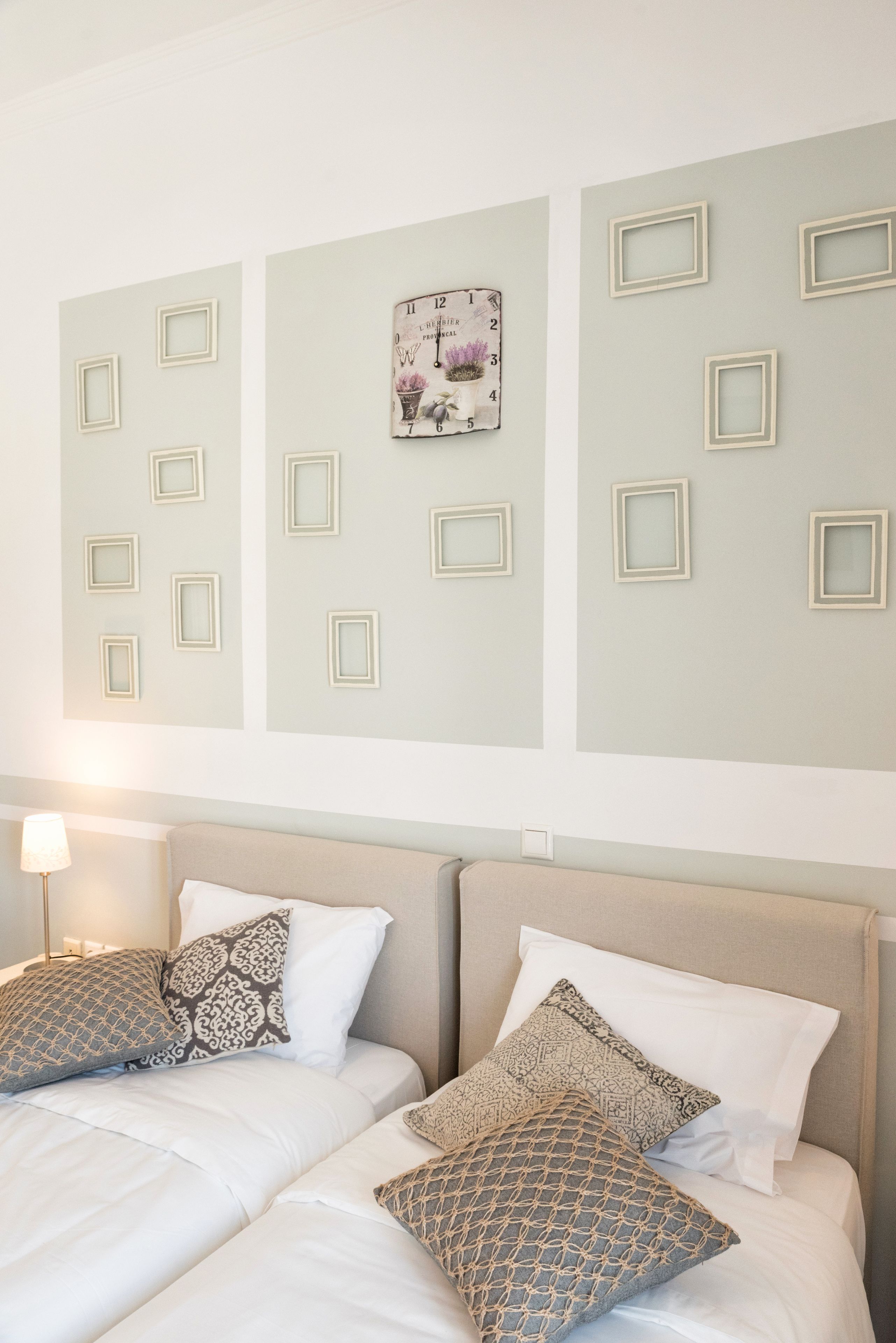 Quarto de hotel com duas camas, um relógio na parede e quadros emoldurados.