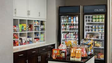 Uma área de lanches e bebidas com serviço próprio, com seções refrigeradas identificadas como 'COLDER' e prateleiras abastecidas com lanches e bebidas.