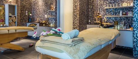 Sala de spa com mesa de massagem, toalhas e prateleira com produtos de higiene pessoal.