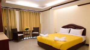 Quarto de hotel com uma cama grande, uma mesa pequena com cadeiras e uma janela com cortinas.