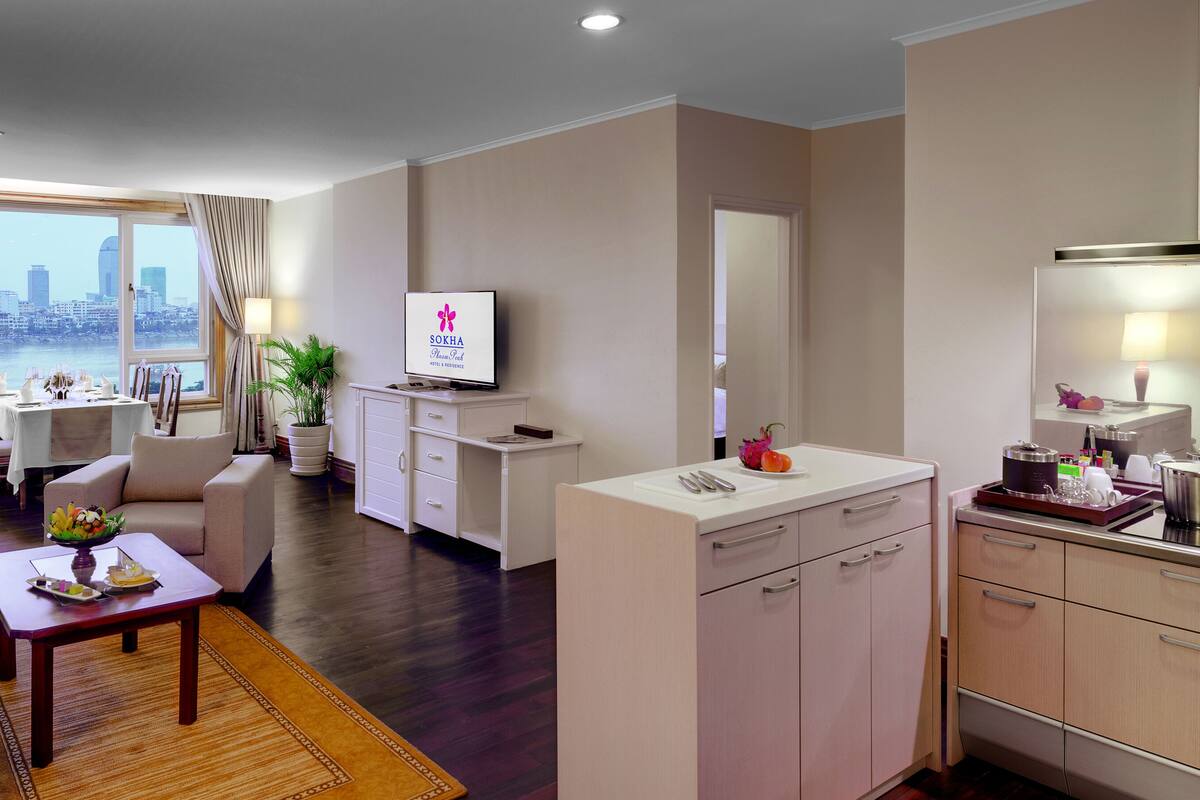 Quarto de hotel moderno com área de jantar, cozinha compacta e uma grande janela com vista para a cidade.